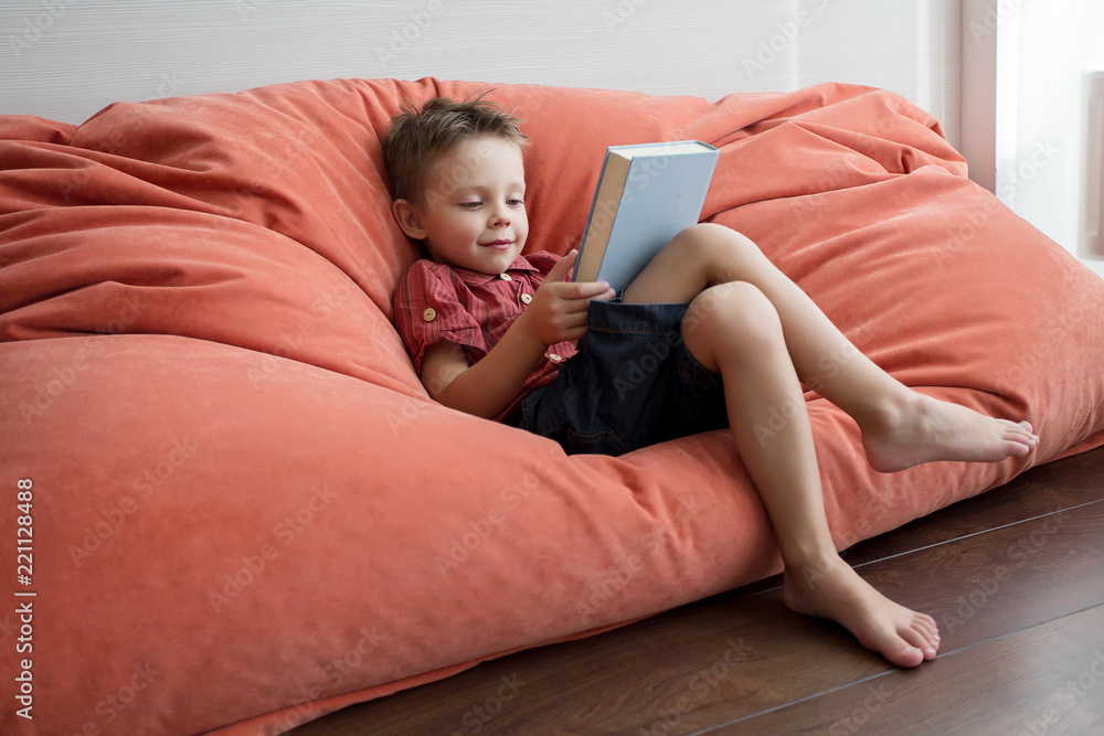 A cute preschool boy sitting reading a book on a soft chair. Stock ...