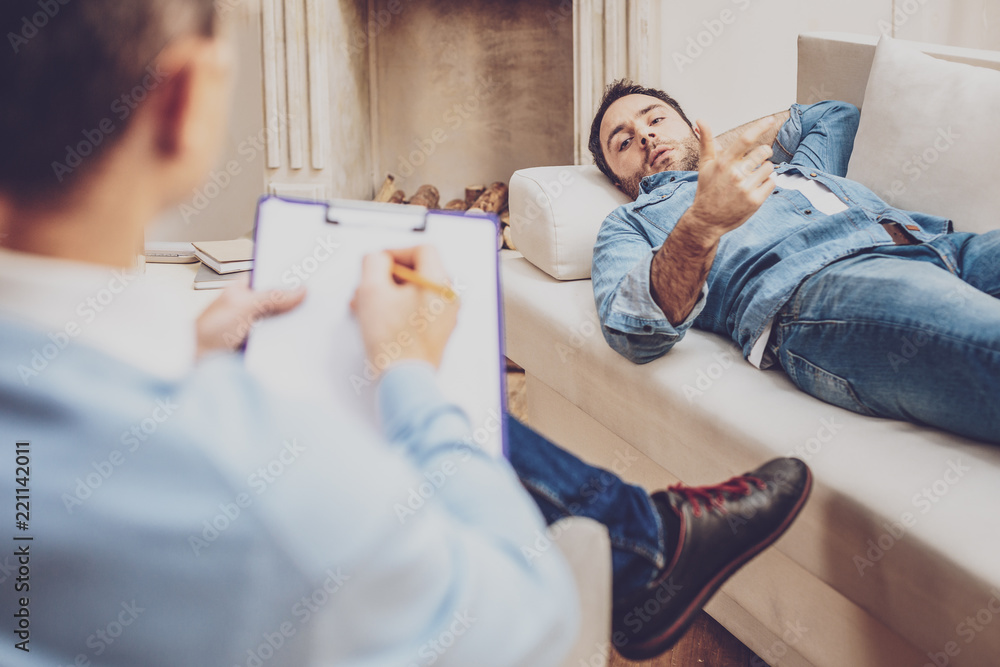 Visit to the psychologist. Cheerless young man lying on the sofa while ...