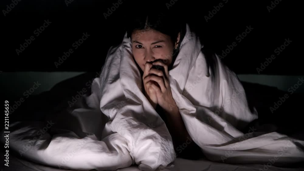Woman watching horror movie alone in bed. Asian woman lying in bed ...