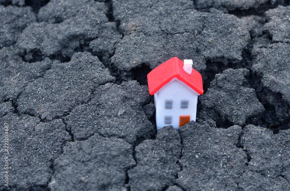 Miniature toy house in dry cracked earth. Natural disasters and ...