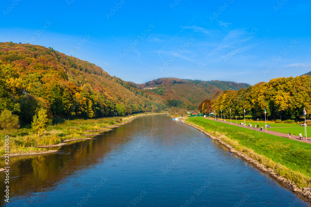 Beautiful scenery of the river Weser in autumn with the colourful trees, the blue sky and the ...