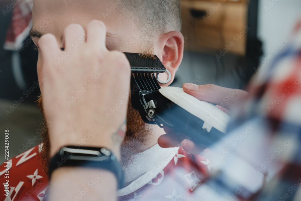Handsome bearded bald man in barbershop. Barber cuts hair with trimmer ...