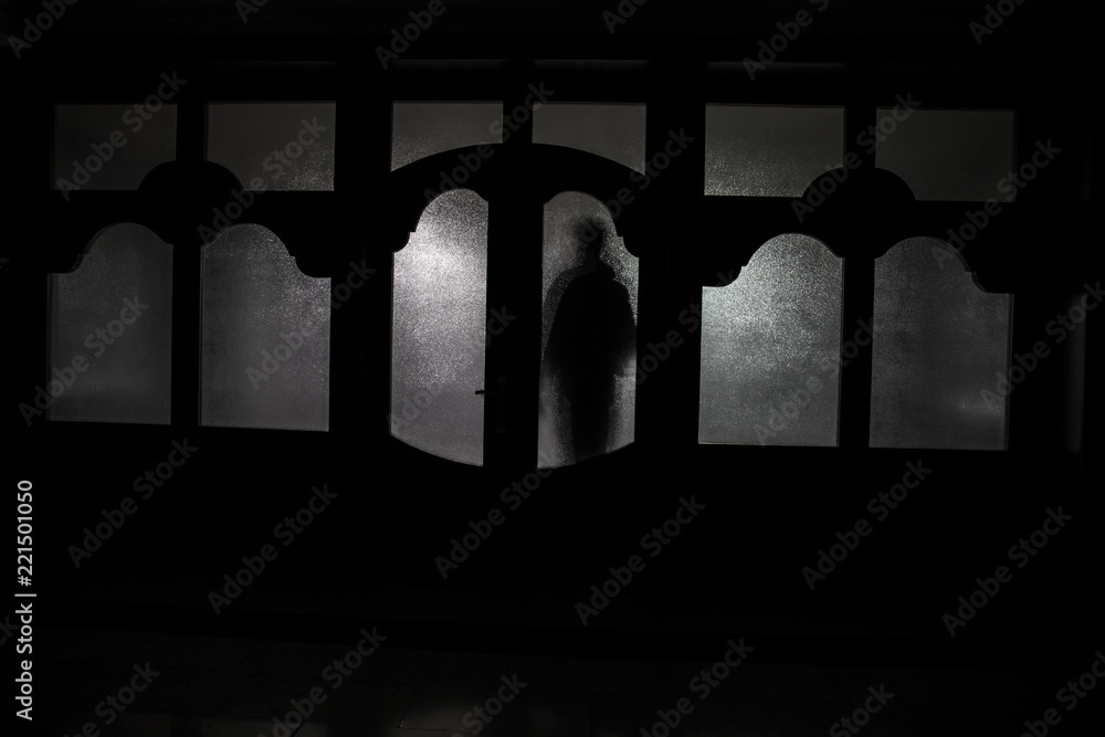 Silhouette of an unknown shadow figure on a door through a closed glass ...