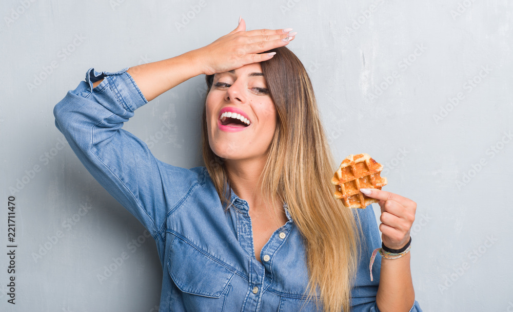 Young adult woman over grey grunge wall eating Belgium waffle stressed ...