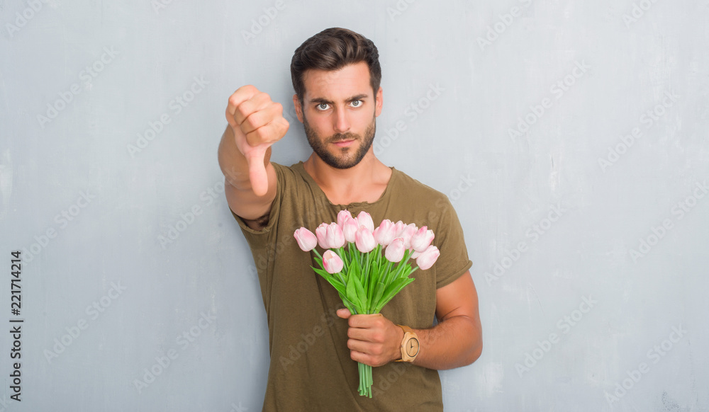 Handsome young man over grey grunge wall holding flowers bouquet with ...