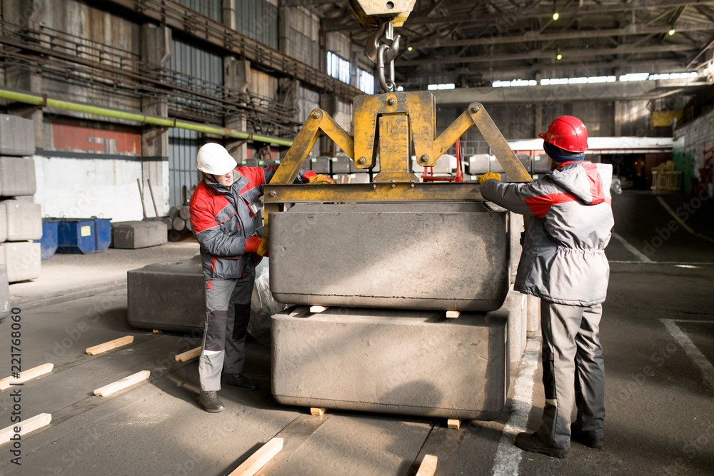 Full length portrait of two factory workers moving loads while using ...