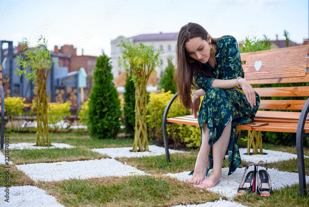 Young woman sitting on bench barefoot next to high heel shoes, rest ...