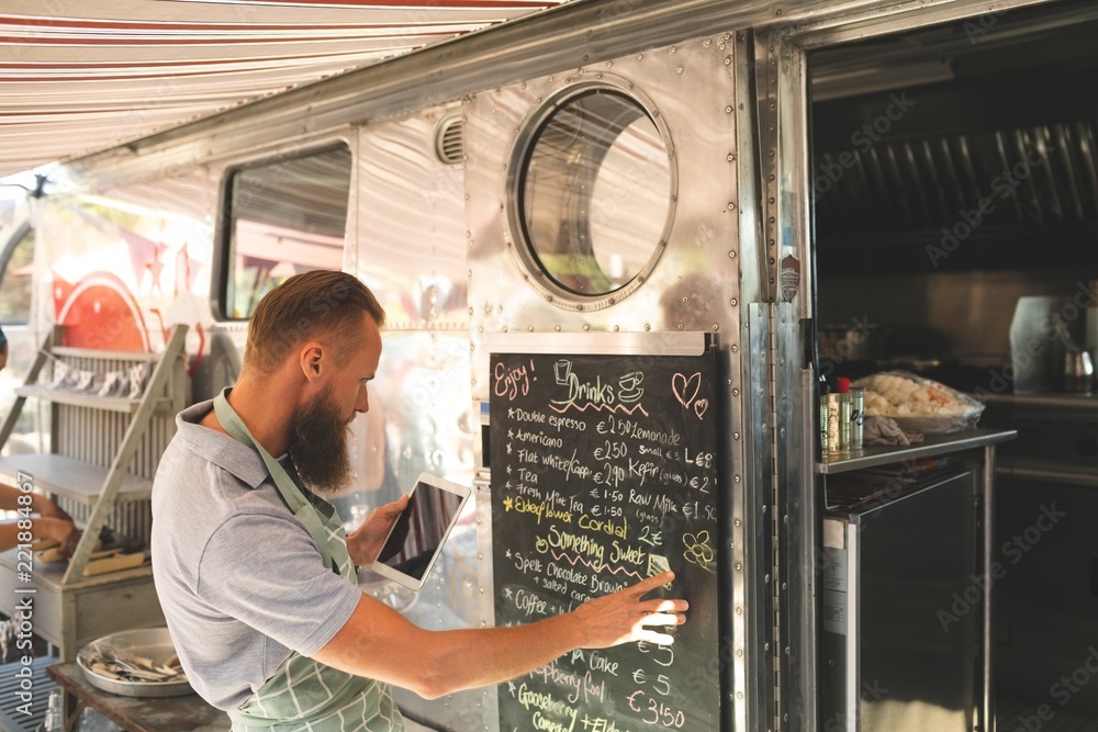 Male waitress writing menu on menu board while using digital Stock ...