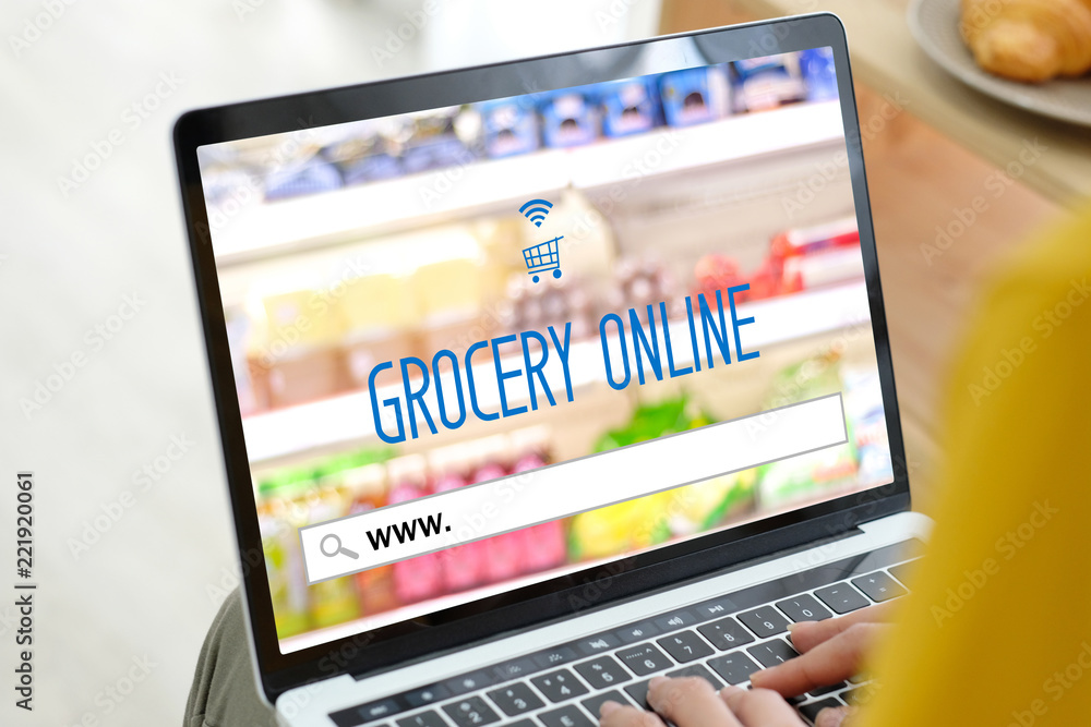 Hand tying laptop computer with www. on search bar over blur grocery ...