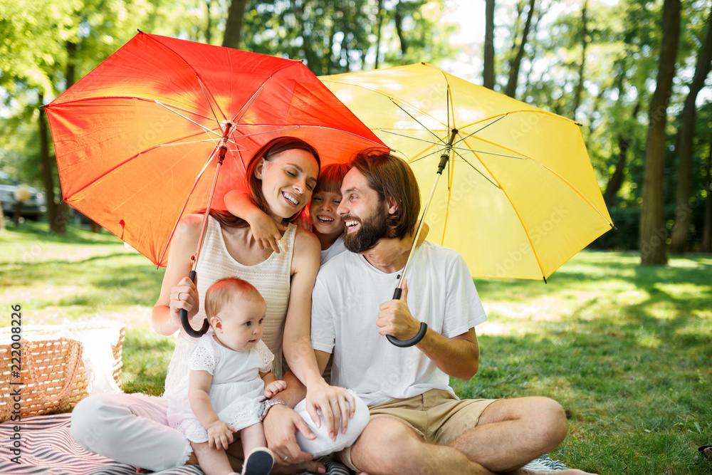 Happy parents with two kids have a rest on the lawn under the bright ...