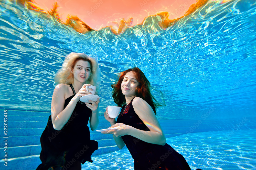 Two charming young girls swimming and posing underwater in the pool ...