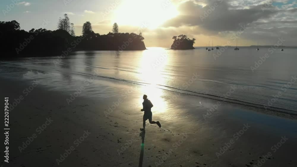 Cinematic aerial tracking shot of silhouetted young man running on a ...
