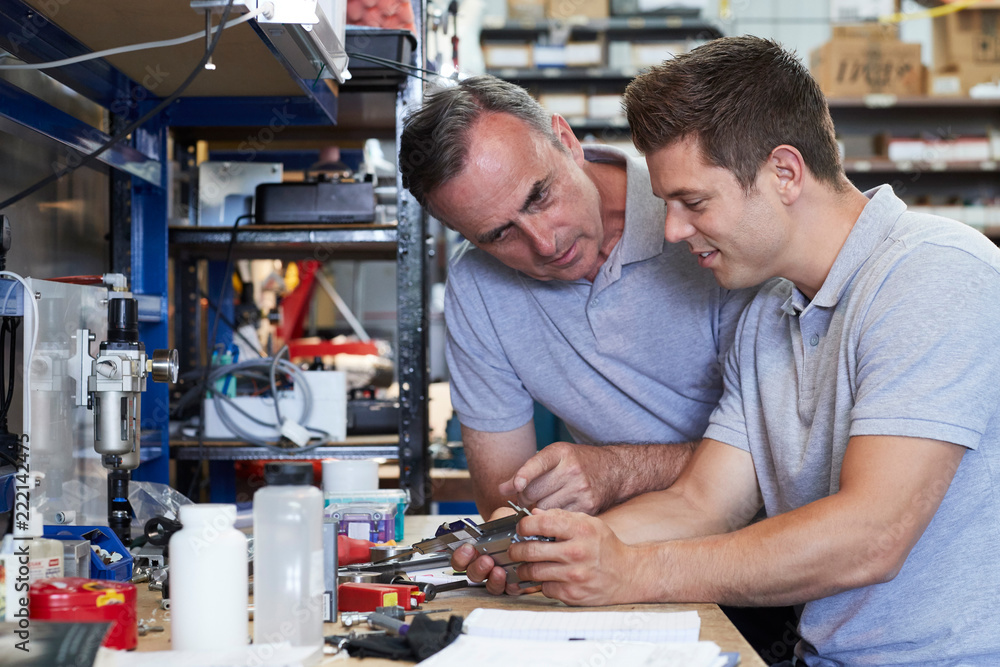 Engineer Helping Male Apprentice In Factory To Measure Component Using ...
