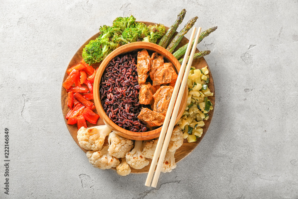 Tasty boiled wild rice with meat in bowl and vegetables on light table ...