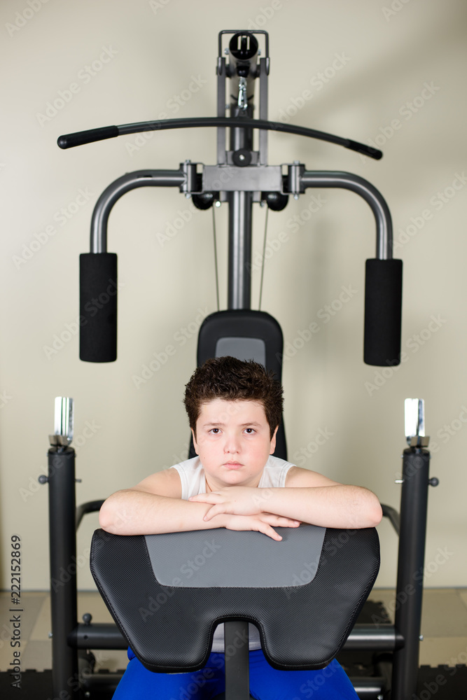 cute fat little caucasian boy sitting on sport exercise machine in ...