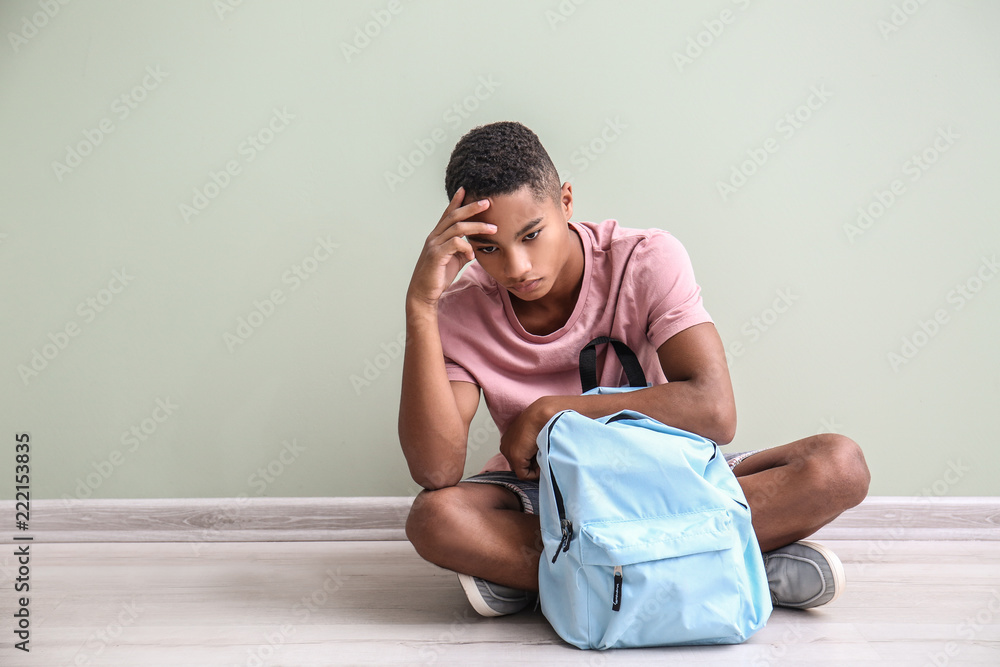 Sad African-American teenage boy sitting on floor indoors. Bullying at ...