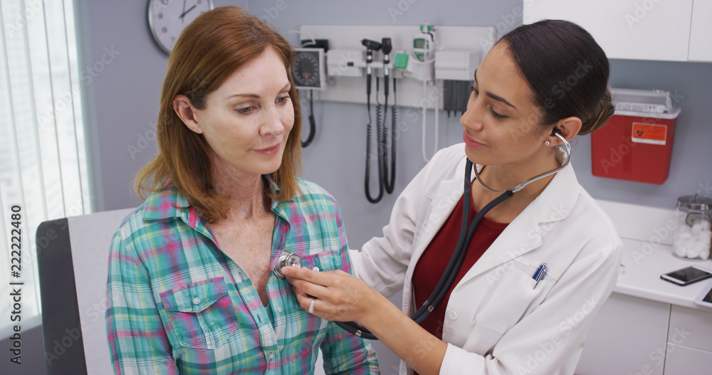 Lovely young latina doctor using stethoscope to examine senior patients ...