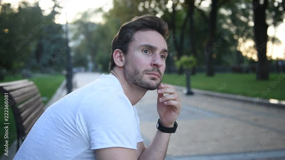 A sad handsome man sitting on a bench waiting for someone on a sunny ...
