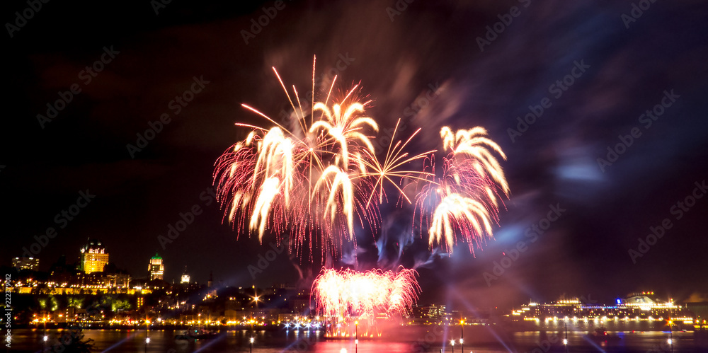 Bright falling fireworks in a dark sky over the water of a big river in ...