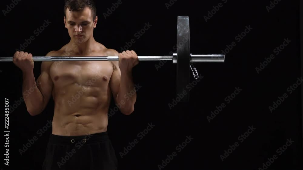 Man is doing exercises with a barbell, training on a black background ...