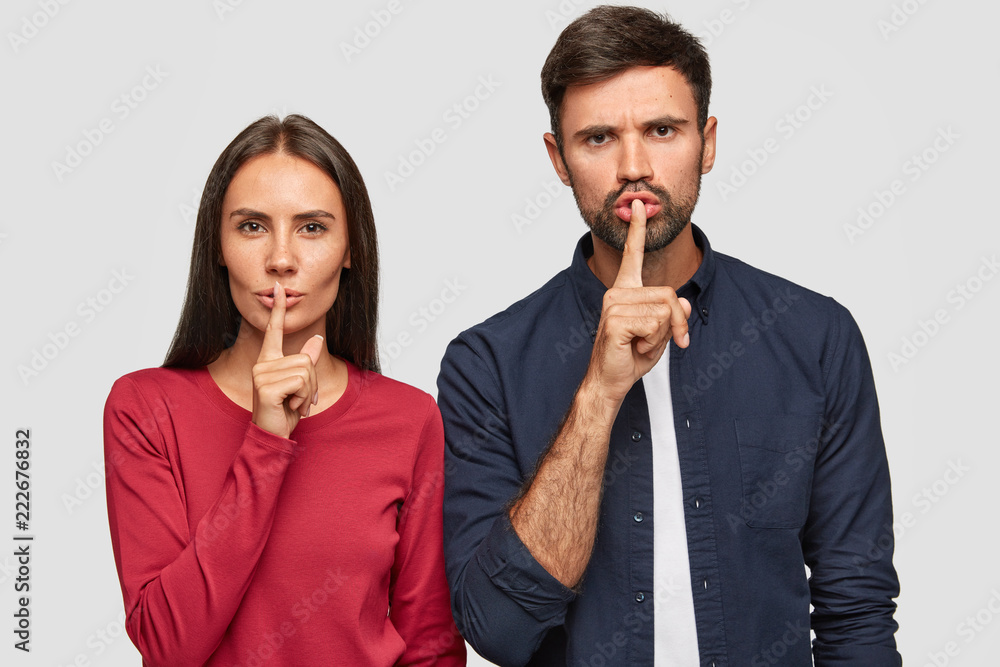 Studio shot of secret young Caucasian woman and man keep index fingers ...