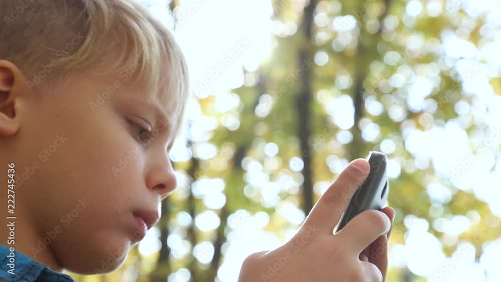 Closeup profile view of cute blond white kid using modern mobile ...