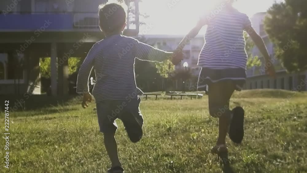 Happy kids holding hands and running together on lawn. Little boy and ...