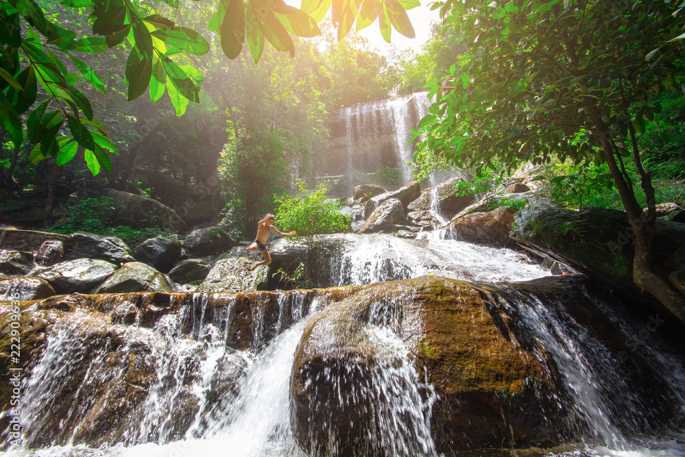 Boy is jumping into a waterfall in forest at Soo Da Cave Roi et ...
