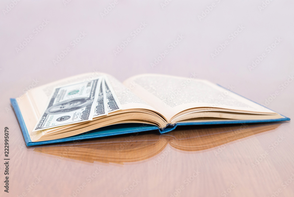Open book on a glassy table with 100 us dollar banknotes on the page ...
