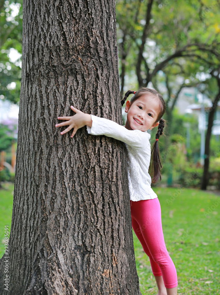 Portrait of cute little child girl hugging tree in the park. Stock ...
