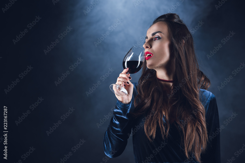 beautiful vampire drinking blood from wineglass on dark background with ...