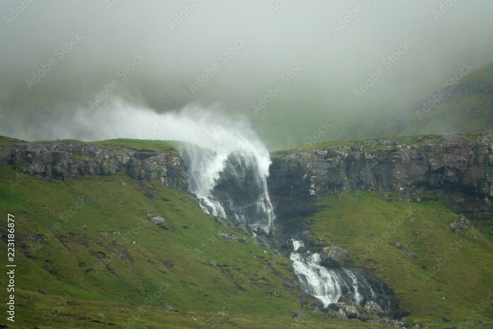 Strong gusts of wind blow past a mountain stream and spray water in the ...