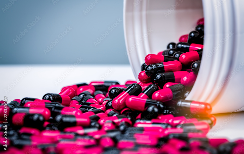 Pink, black capsules pill spilled out from white plastic bottle ...