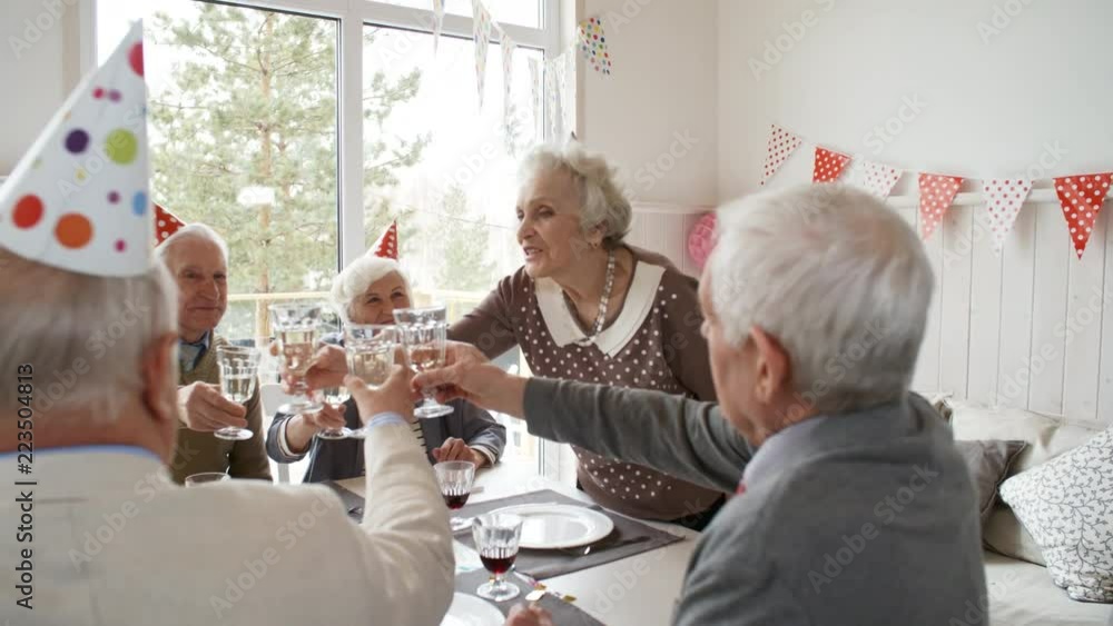 Joyous senior woman in party hat saying thanks to guests at celebration ...