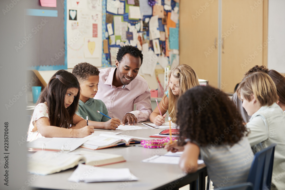 Male teacher works with elementary school kids at their desk Stock ...