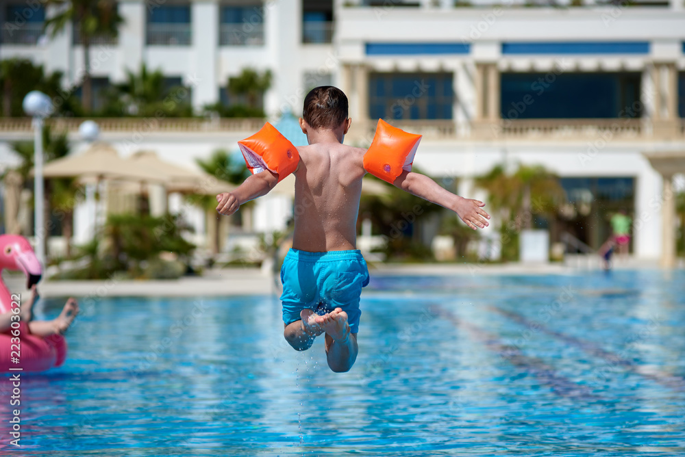 Caucasian boy spending time in pool at resort. He is making high jump ...