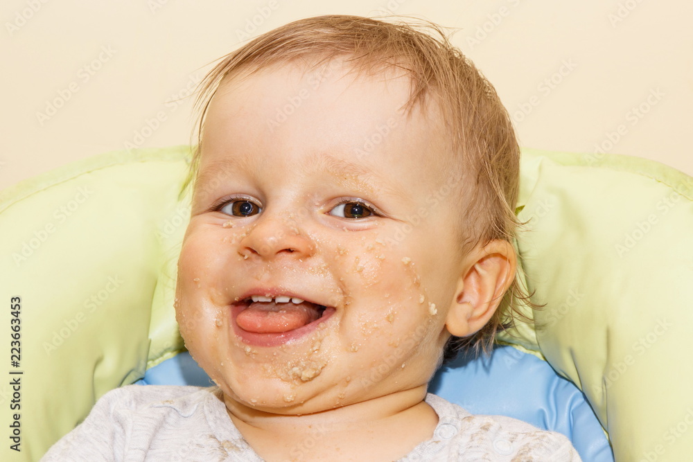 Happy little child with dirty face eating porridge or oatmeal for ...
