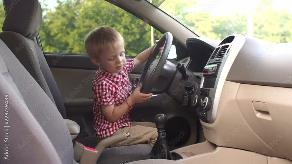 Little cheerful boy sits playing behind the wheel of a car. Portrait of ...