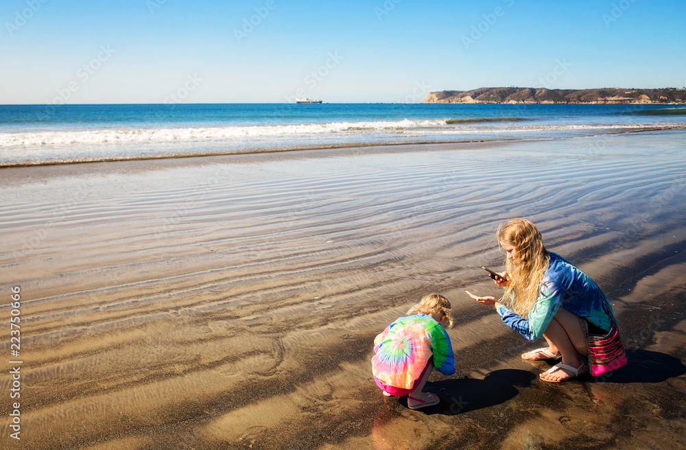 A teenage girl and her little sister squatting on the beach exploring ...