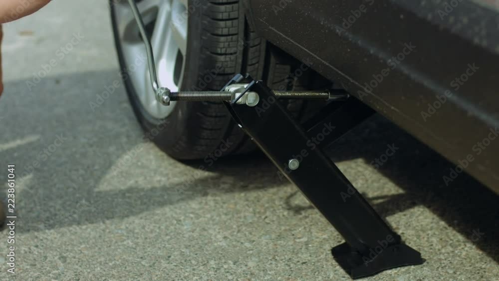 Close-up of male hand lifting car with spanner jack-screw to change ...