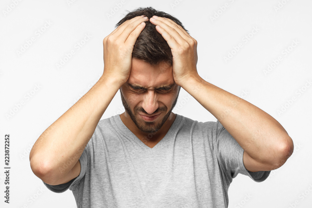 Young man isolated on gray background, showing how much his head hurts ...