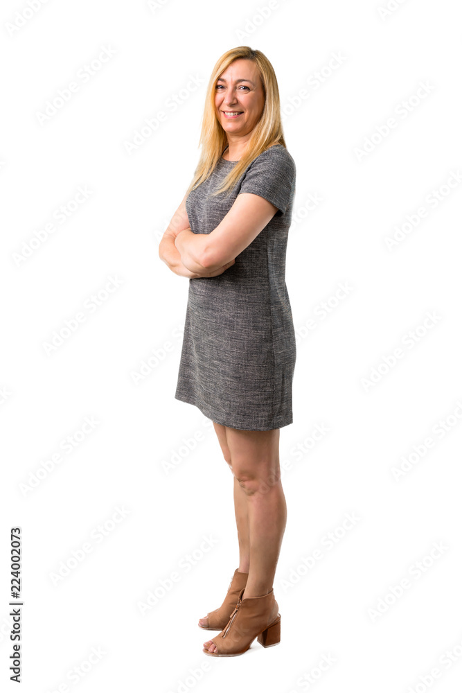 Middle age blonde woman with grey dress keeping the arms crossed in lateral position while ...