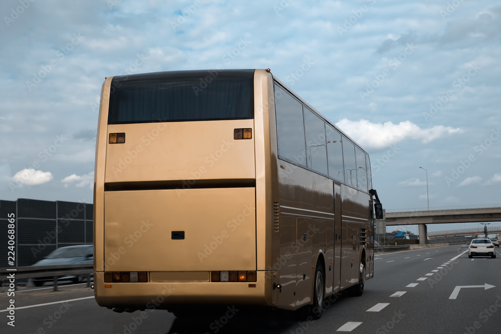 Gold intercity bus is driving along the road. Back view. Sunny day. The ...