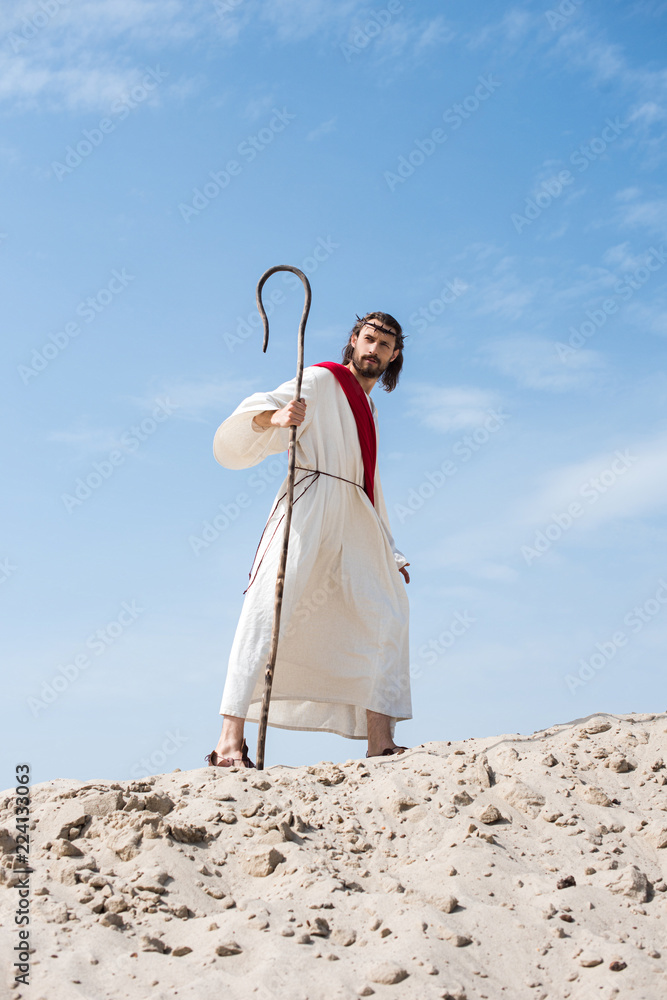 Jesus in robe, red sash and crown of thorns walking on sandy hill with ...