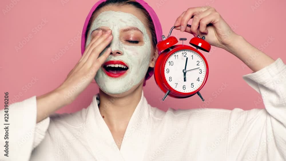 Vidéo Stock Sleeping Girl With A Mask On The Face And A Towel On His Head Holds The Alarm Clock