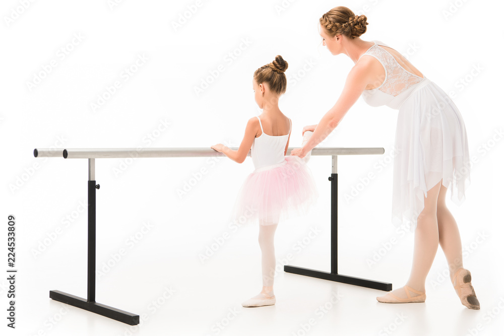 rear view of adult female teacher in tutu helping little ballerina ...