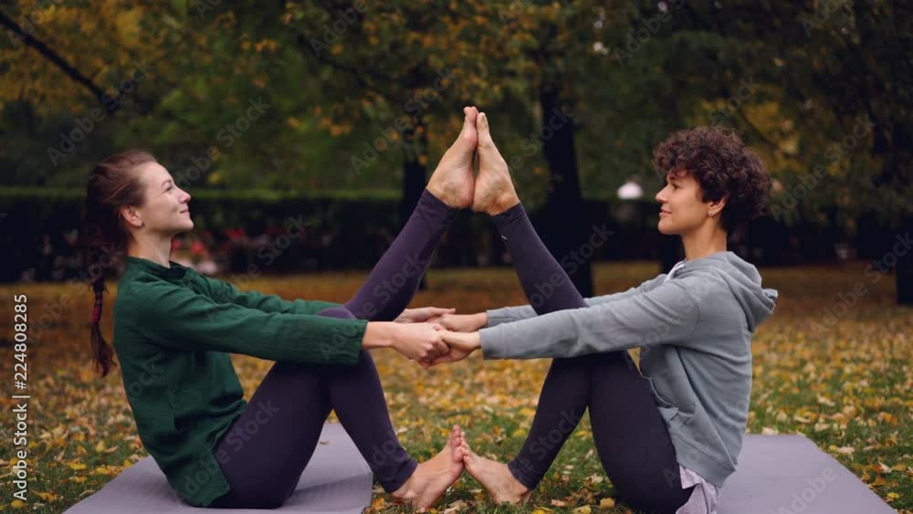 Attractive girls are doing yoga exercises in pair holding hands and ...