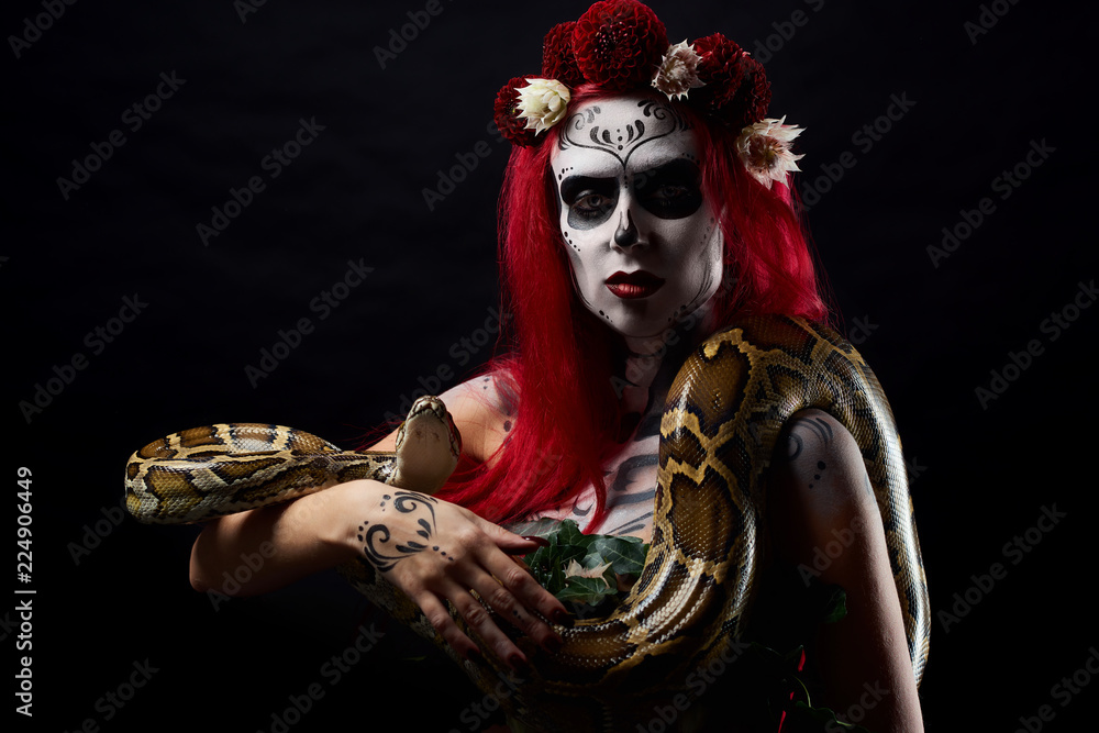 Monster woman with drawing face and flowers on head holding long snake ...