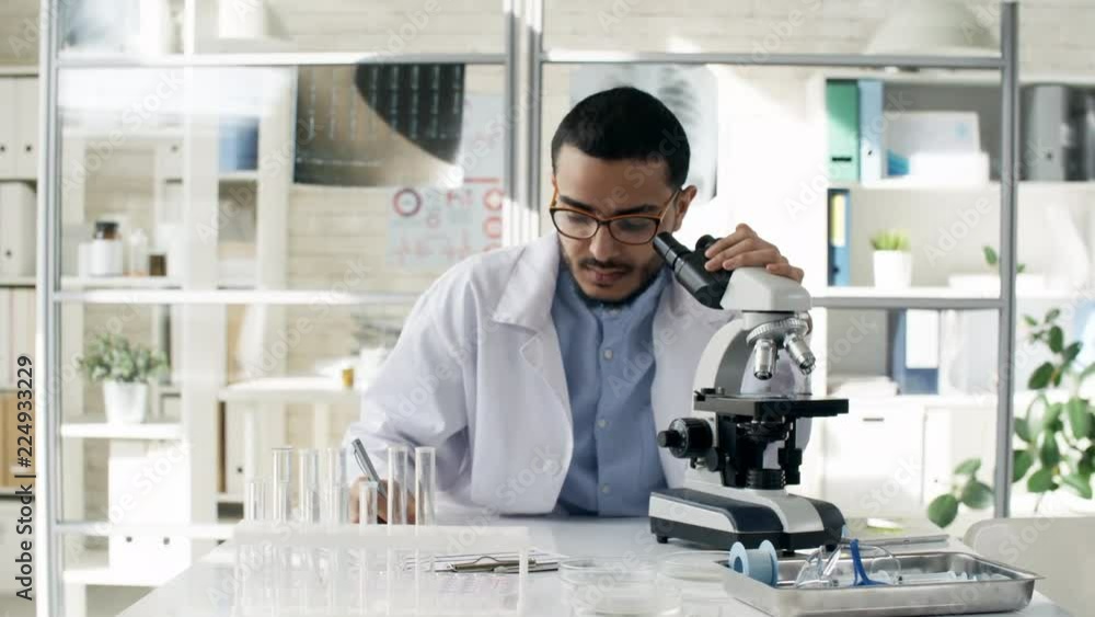 Zoom in shot of focused young black man in lab coat and glasses using ...