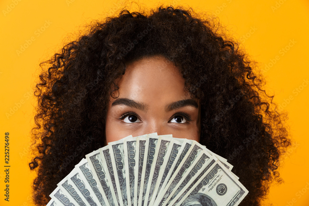 Woman posing isolated over yellow background holding money covering ...